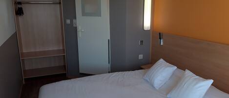 Quarto de hotel com uma cama, um guarda-roupa e uma mesa de cabeceira.