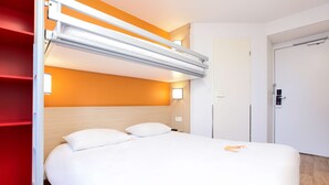 Quarto de hotel com uma cama, um guarda-roupa vermelho, uma porta branca e um candeeiro fixo na parede.