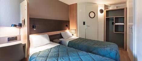 Quarto de hotel com duas camas, uma escrivaninha, um guarda-roupa e um banheiro.