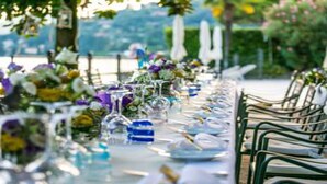 Mesa longa posta para um evento formal, com cadeiras em ambos os lados, decorada com flores e taças.