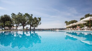 Piscina azul límpida com espreguiçadeiras e guarda-sóis, cercada por árvores.