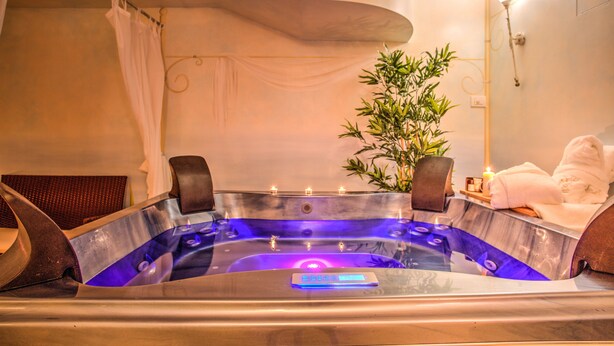 Uma banheira de hidromassagem com painel de controle, uma planta em vaso e um porta-toalhas.