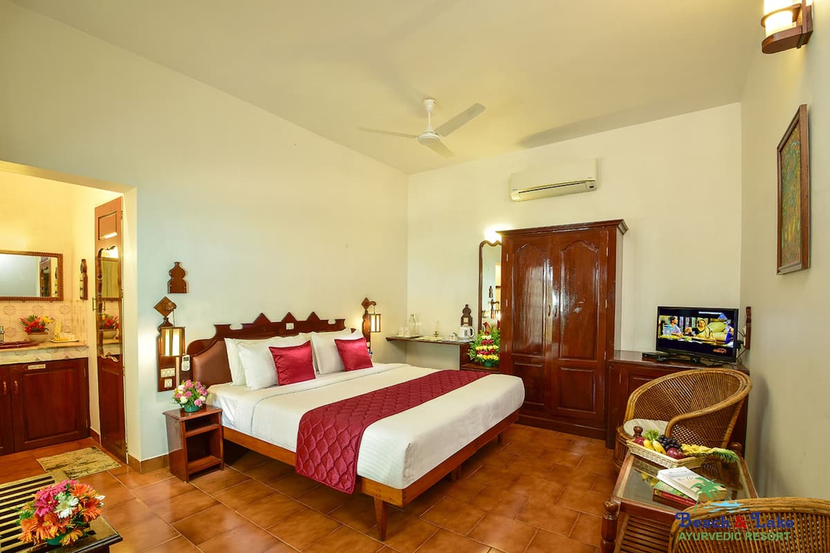 Quarto de hotel com cama, televisão, cadeira de vime, mesa pequena e guarda-roupa de madeira.