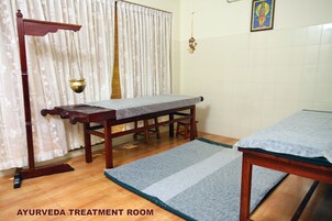 Sala de tratamentos ayurveda com uma mesa de madeira, um tapete e uma cortina.