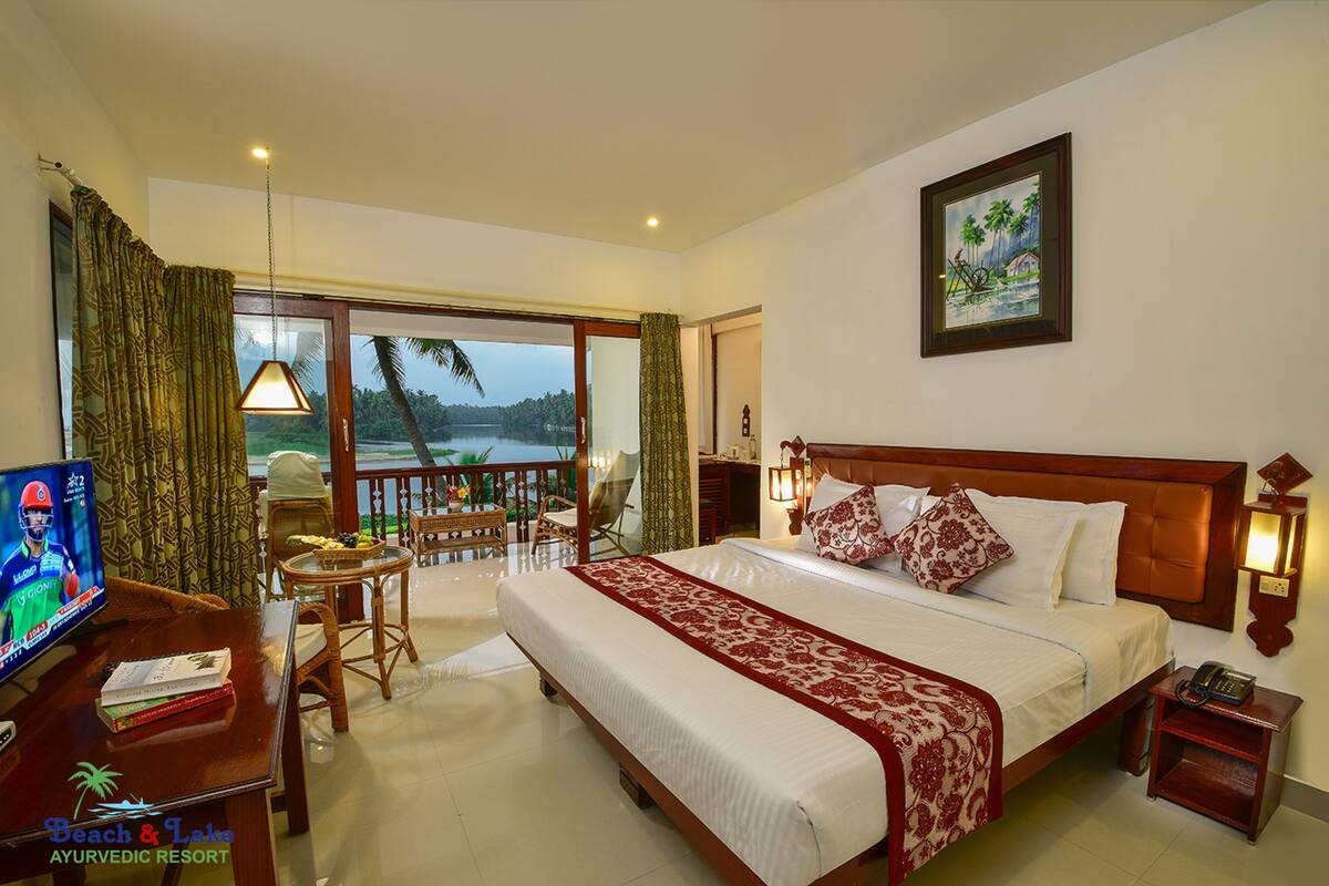Quarto de hotel com uma cama grande, televisão, escrivaninha com cadeira e varanda com vista para a água.