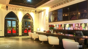 Uma área de bar com um balcão extenso, vários banquetas brancas e uma variedade de garrafas.