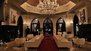 Um salão imponente com um grande candelabro, janelas em arco e um tapete vermelho que conduz a uma área de estar.