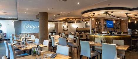 Um restaurante moderno com área de bar, mesas de madeira e cadeiras brancas.