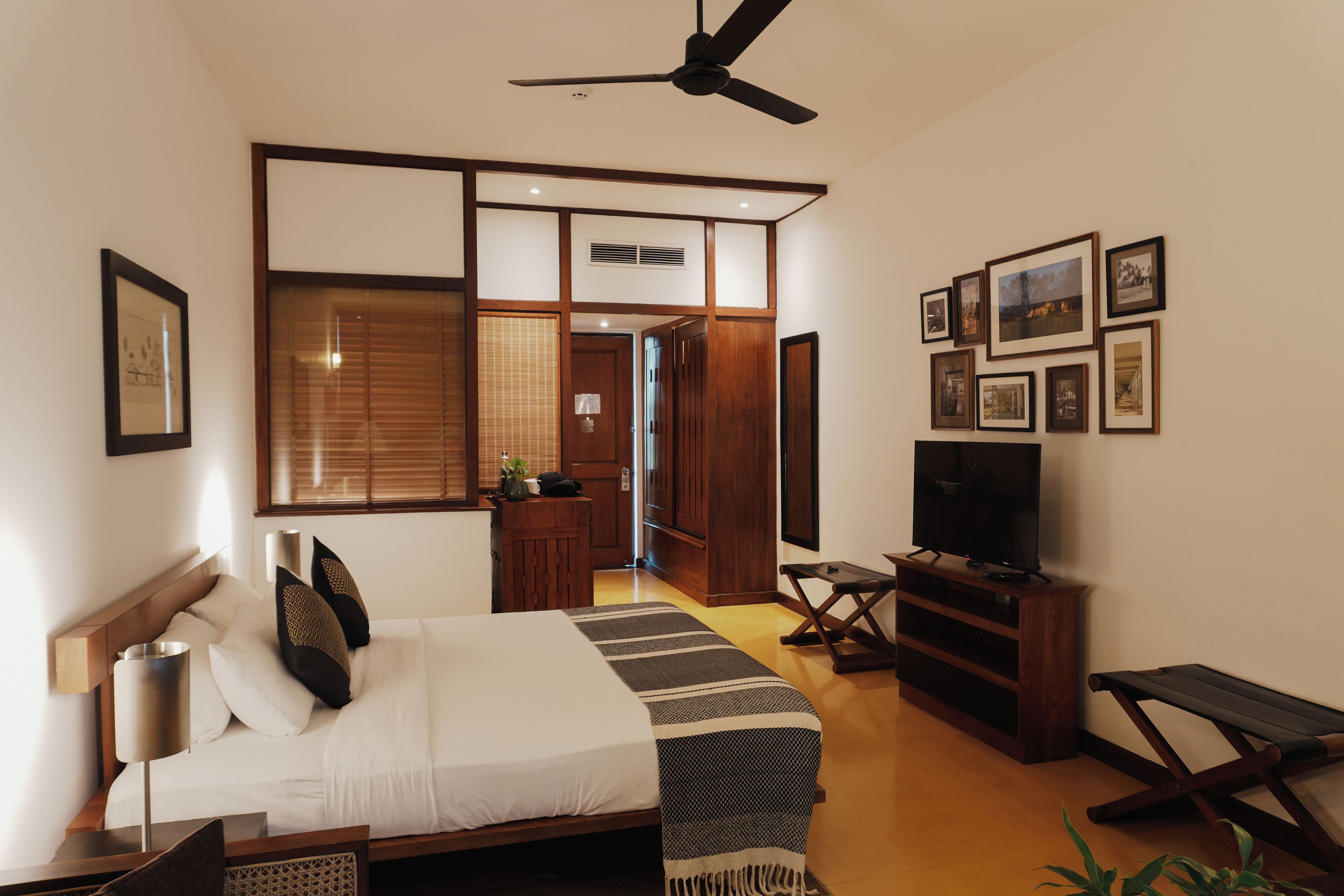 Quarto com cama, televisão, ventoinha no teto e quadros nas paredes.