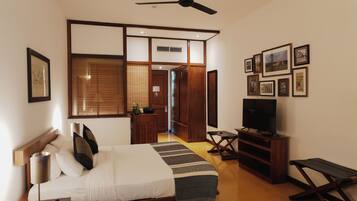 Quarto com cama, televisão, ventoinha no teto e quadros nas paredes.
