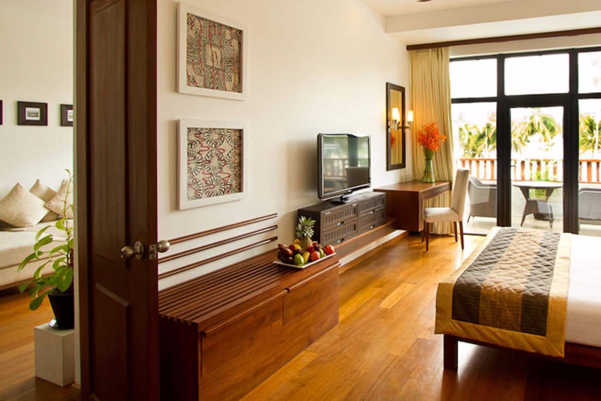 Quarto de hotel com cama, televisão, escrivaninha, varanda e sofá.