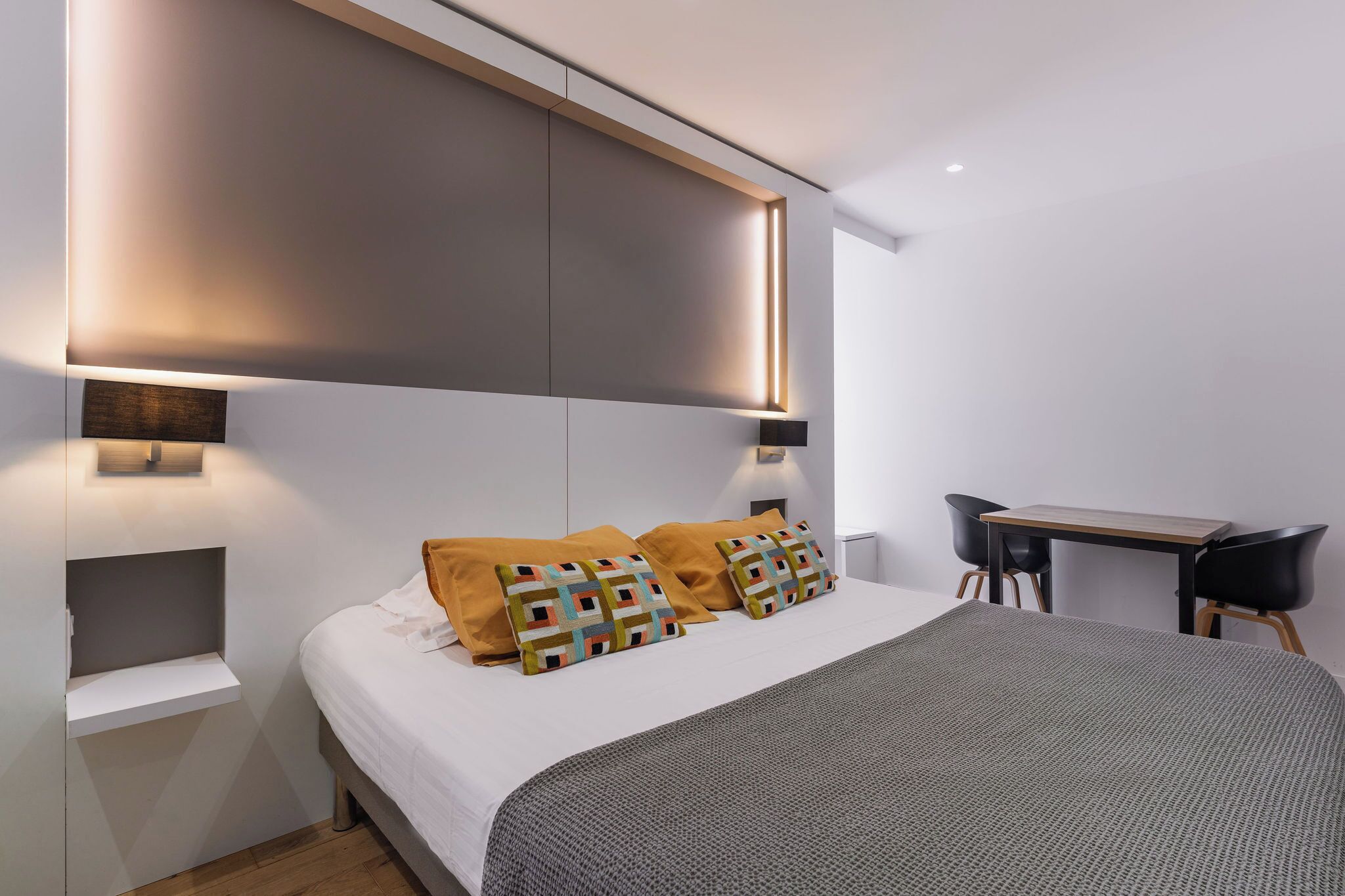 Quarto moderno com cama, mesas de cabeceira, escrivaninha e cadeiras.