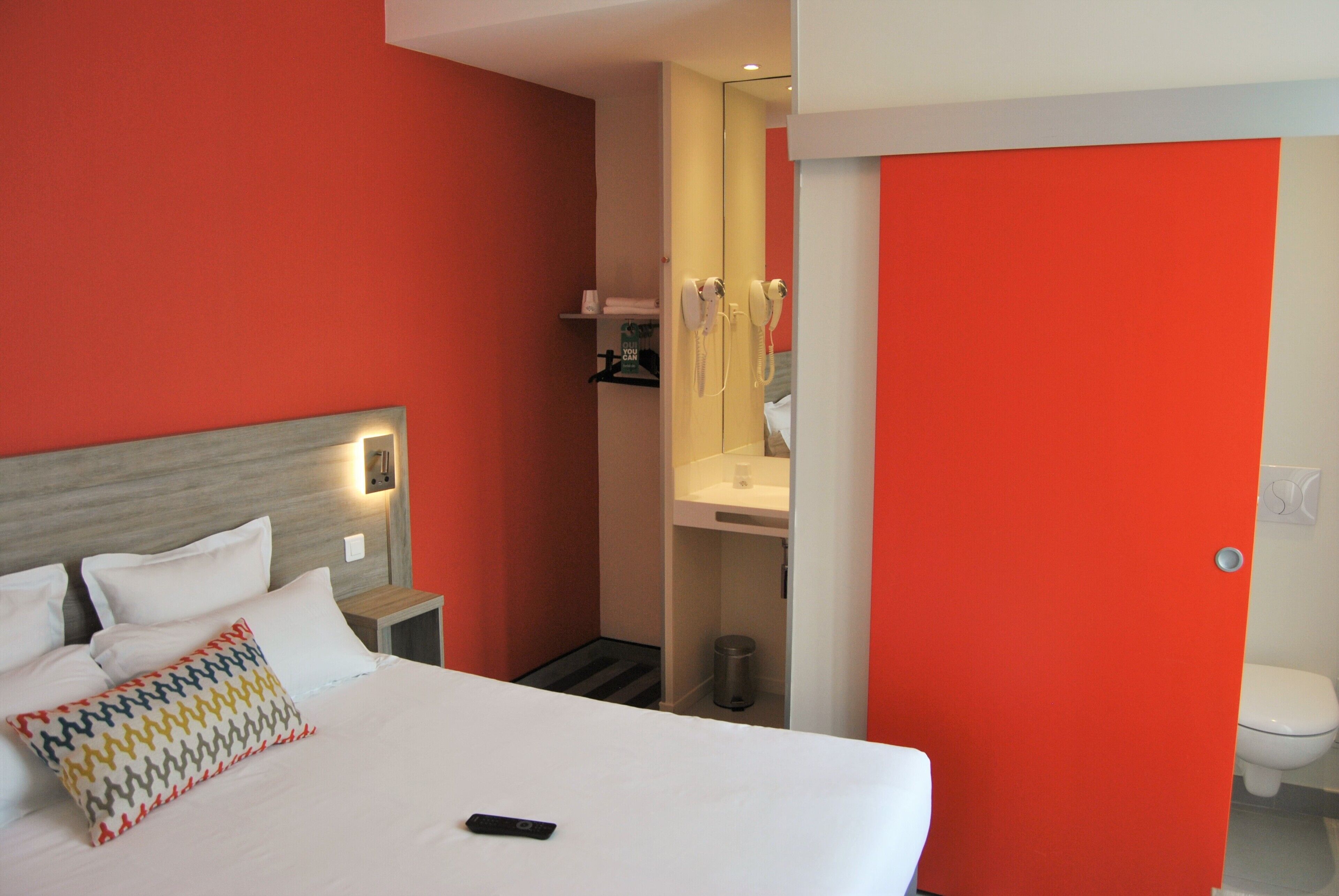 Quarto de hotel com cama, mesa de cabeceira, telefone e banheiro visível por uma porta aberta.