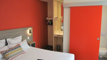 Quarto de hotel com cama, mesa de cabeceira, telefone e banheiro visível por uma porta aberta.