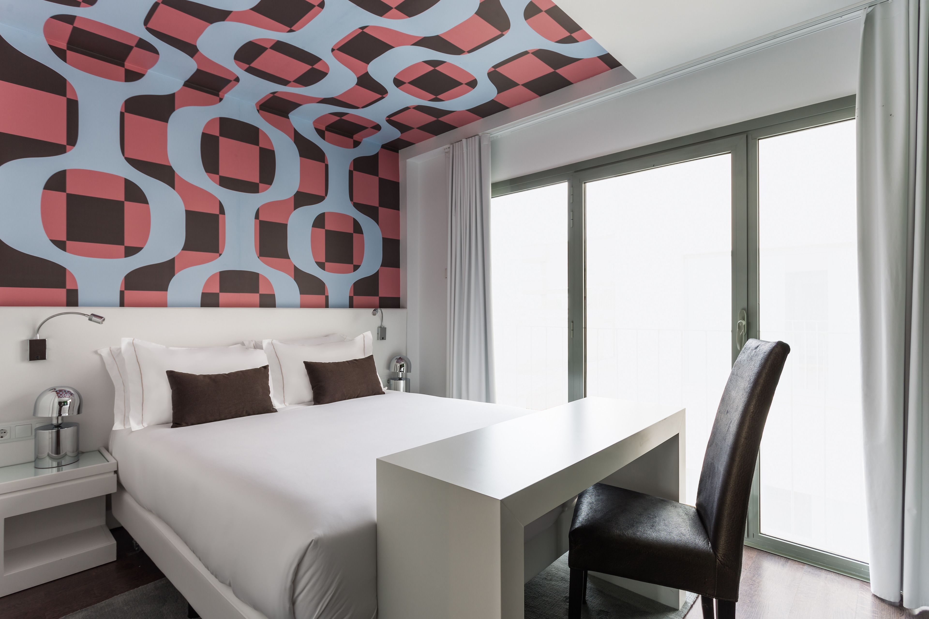 Quarto de hotel moderno com uma cama grande, uma escrivaninha e vista da cidade através de amplas janelas.