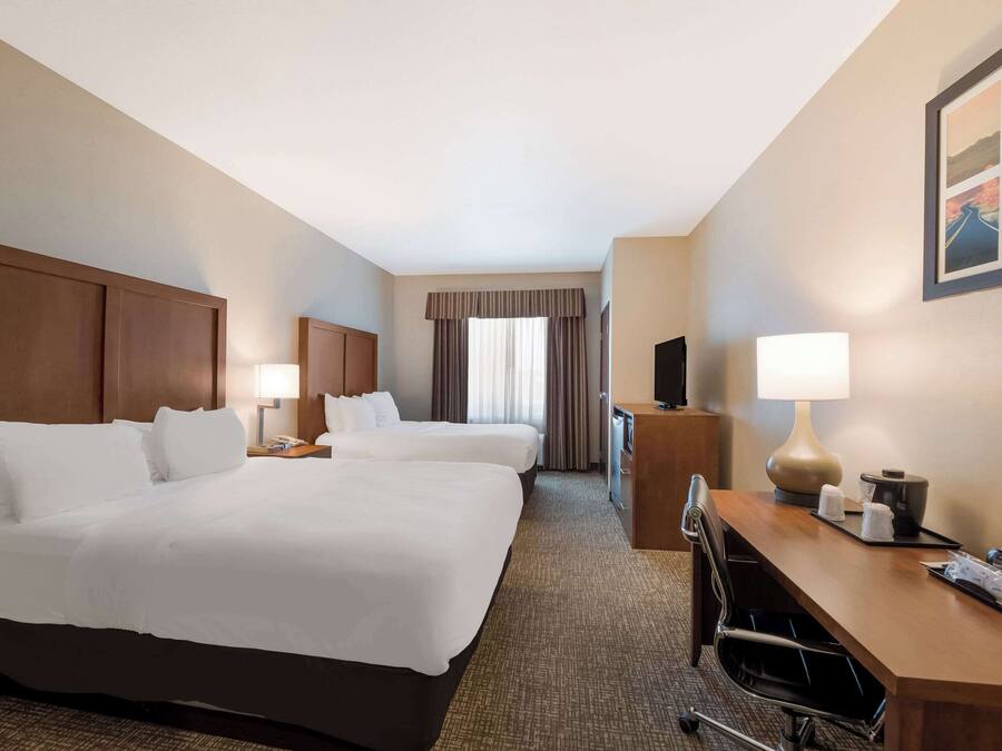 Quarto de hotel com duas camas, uma escrivaninha, uma cadeira, uma televisão e uma janela com cortinas.