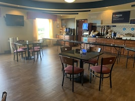 Uma sala de café da manhã moderna com mesas e cadeiras de madeira, uma máquina de café e uma geladeira.
