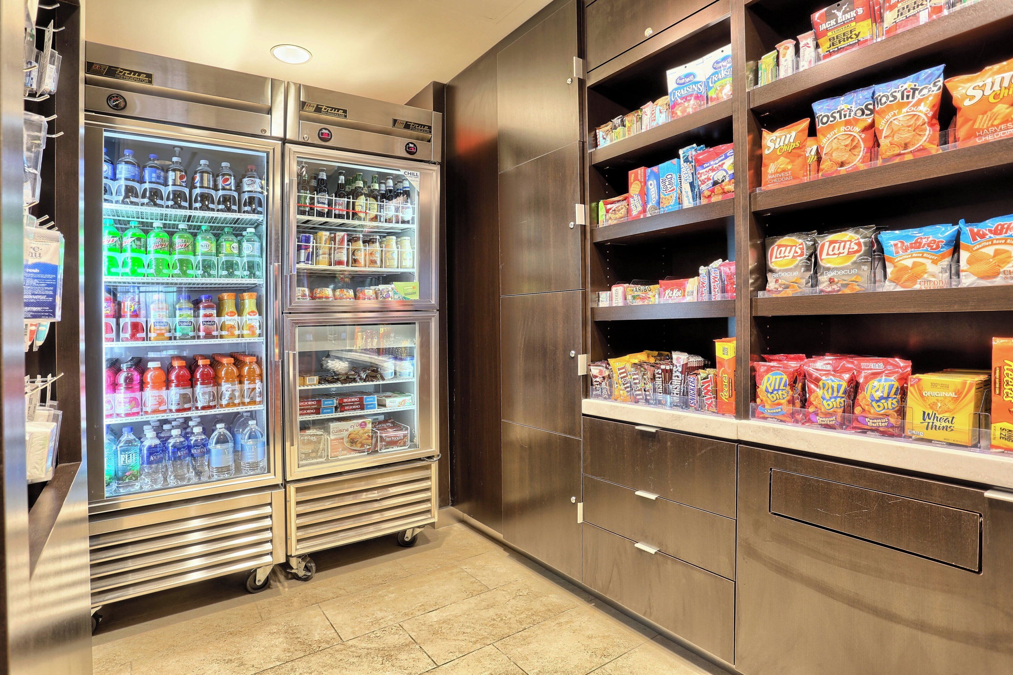 Uma área de distribuição automática com máquinas de bebidas refrigeradas e prateleiras cheias de snacks e cereais.