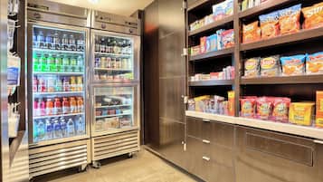 Uma área de distribuição automática com máquinas de bebidas refrigeradas e prateleiras cheias de snacks e cereais.