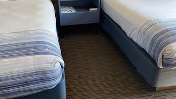 Quarto de hotel com duas camas, uma mesa de cabeceira com luminárias, um telefone e um livro.