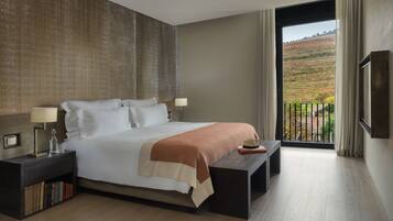 Quarto de hotel moderno com uma cama grande, luminárias de cabeceira, uma mesinha e vista para um vinhedo através de uma varanda.