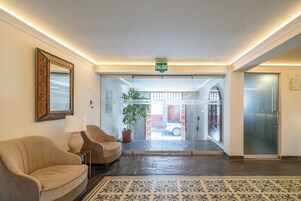 Um saguão de hotel com um balcão de recepção, duas poltronas, um espelho grande, um vaso de planta e um tapete estampado.