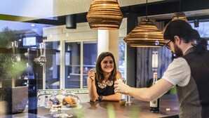 Uma área de bar com luminárias pendentes, uma vitrine de vidro e uma pessoa servindo uma bebida.