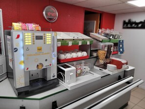 Um espaço com café, máquina de café, chávenas e um relógio a indicar 12:50.