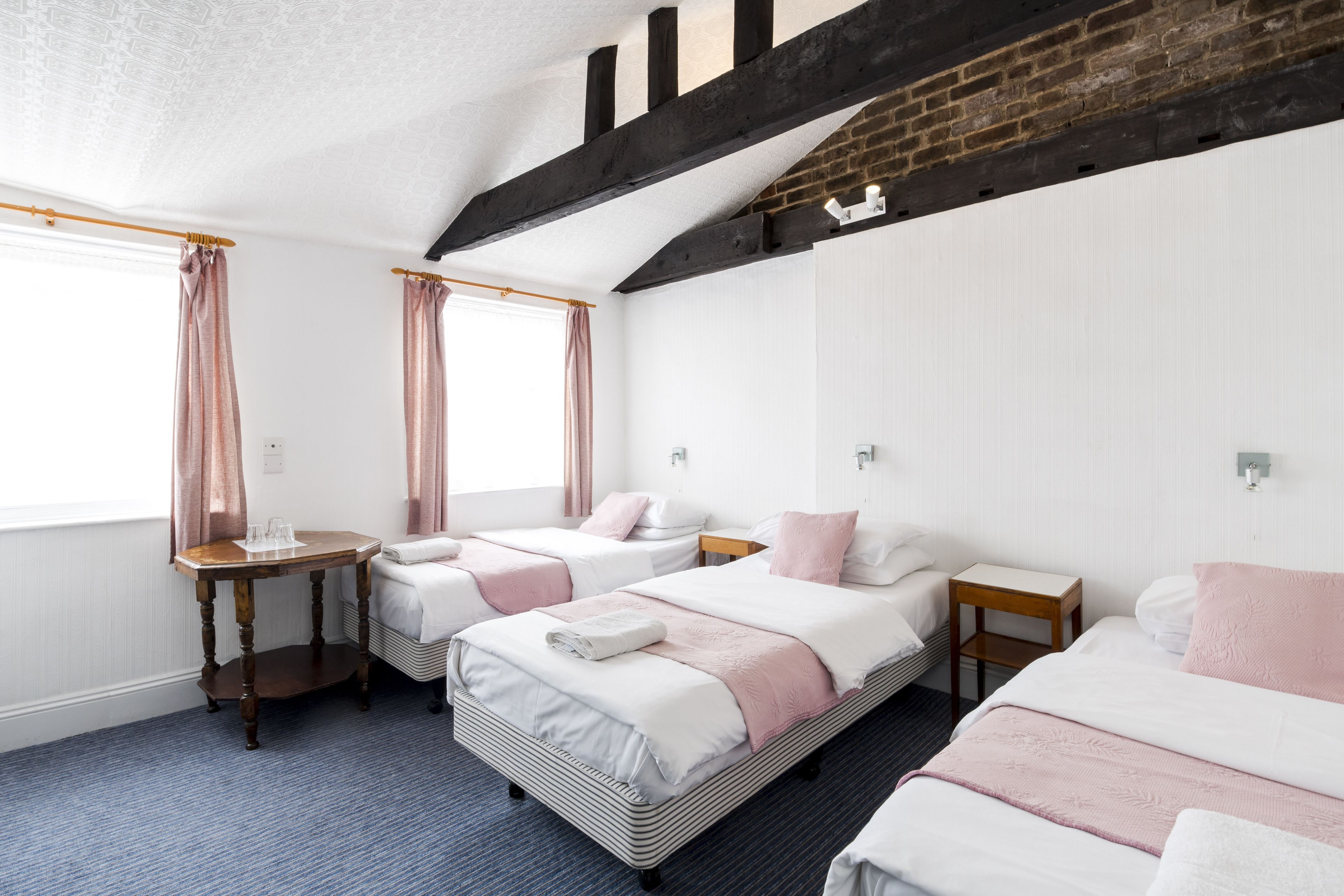 Quarto de hotel com duas camas, uma mesinha e uma janela com cortinas.
