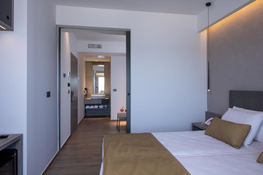 Quarto de hotel moderno com cama, mesa de cabeceira e vista para o banheiro.