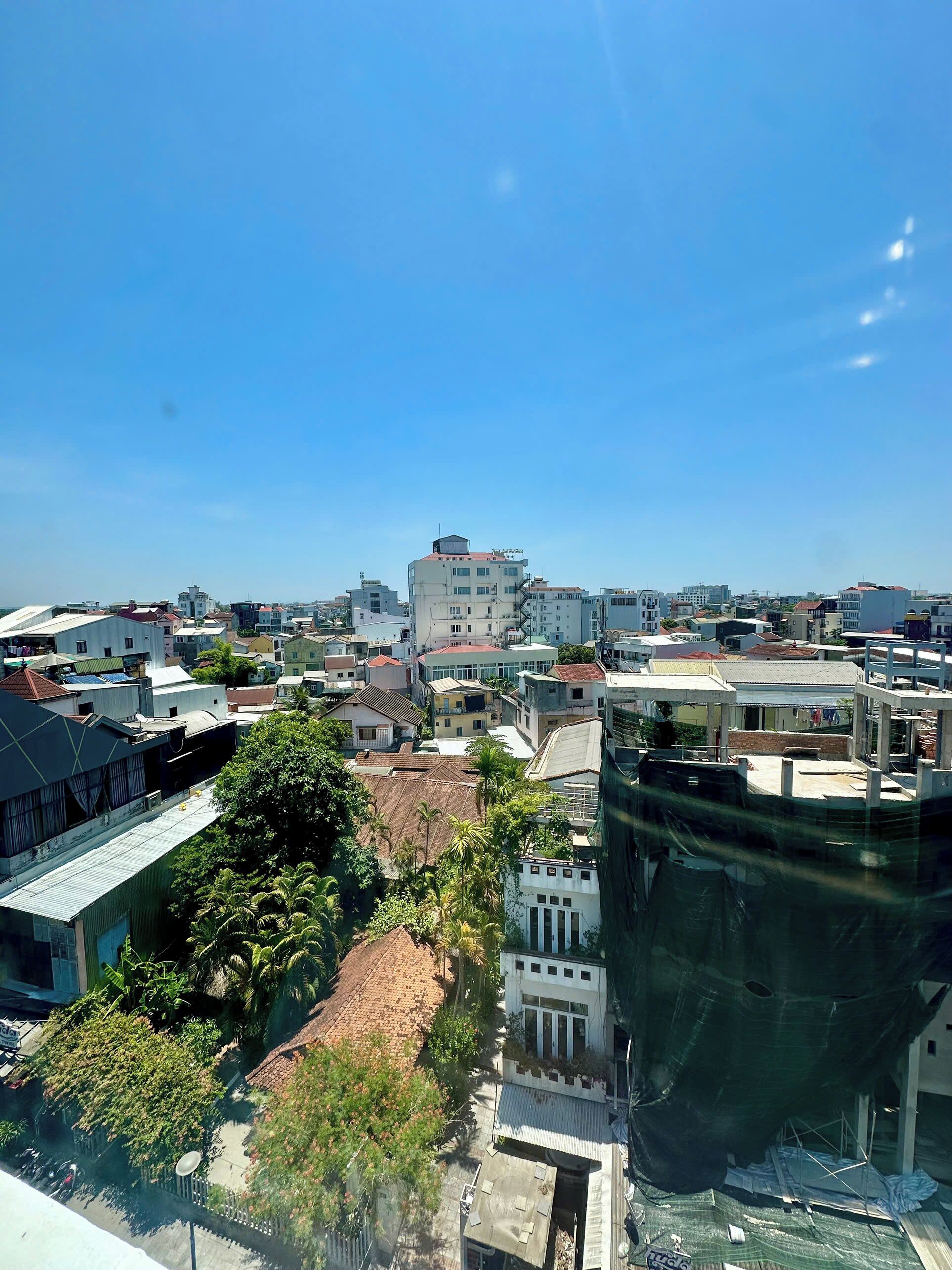 Uma paisagem urbana com diversos edifícios, incluindo uma construção imponente de vários andares com telhado plano e um edifício menor com telhado inclinado.