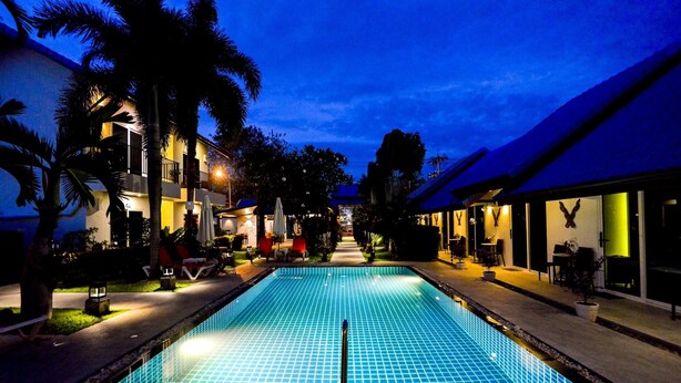 Piscina com deck ladrilhado, cercada por palmeiras e edifícios com área de estar ao ar livre.