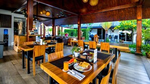 Restaurante com mobiliário de madeira, ventoinha no teto e vista para o jardim.