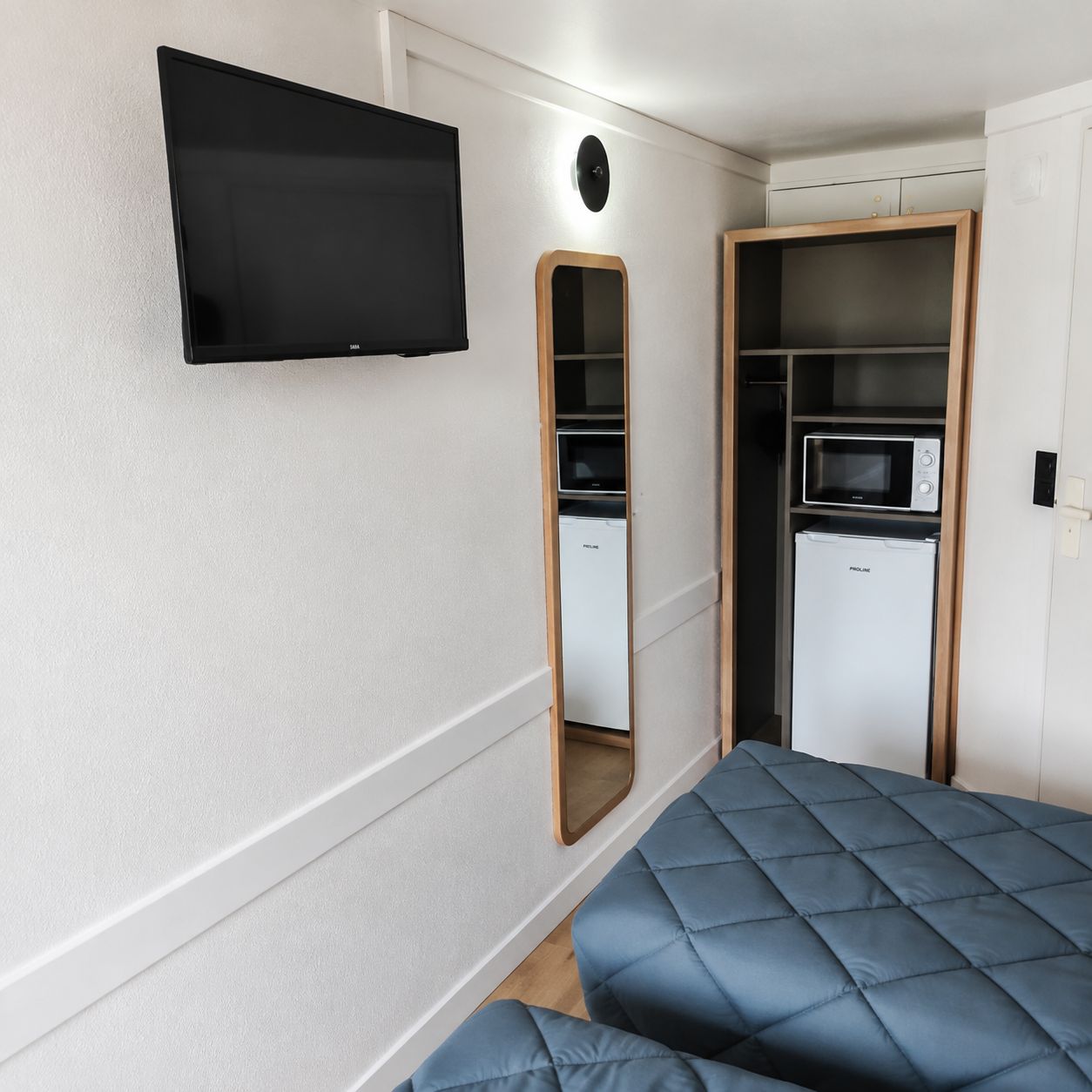Quarto com cama, televisão, guarda-roupa e micro-ondas.