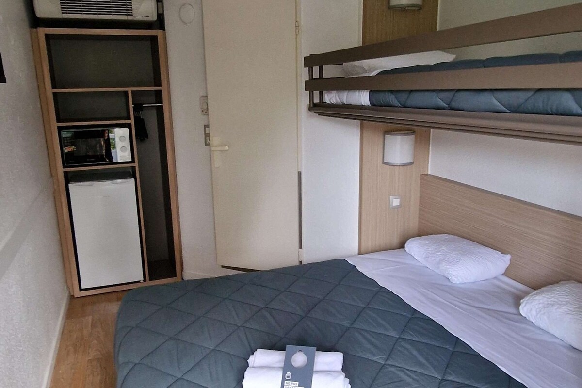 Quarto de hotel pequeno com beliche, kitchenette, guarda-roupa e ar condicionado central.
