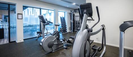 Academia com máquinas de cardio, equipamentos de musculação e vista para uma paisagem nevada através de grandes janelas.
