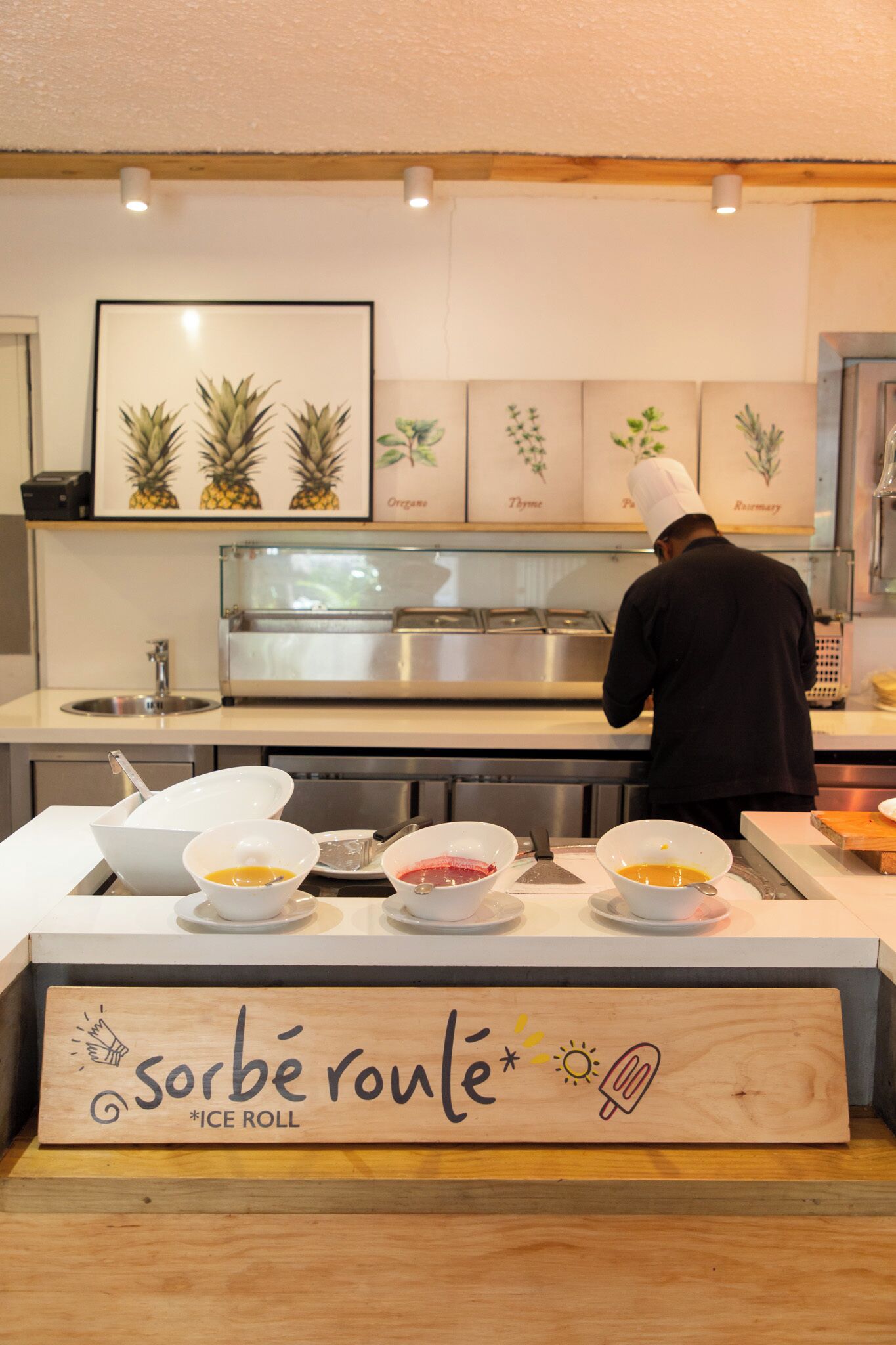 Um chef prepara comida em uma cozinha com uma placa indicando 'Sorbet Roulé' e 'ICE ROLL'.
