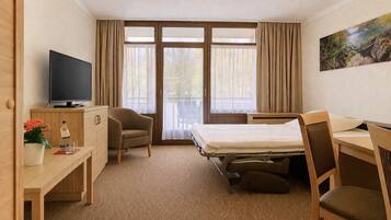Quarto de hotel com cama, escrivaninha, cadeira, televisão e janela com cortinas.