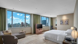 Quarto de hotel moderno com uma cama grande, um sofá, uma televisão e uma escrivaninha.