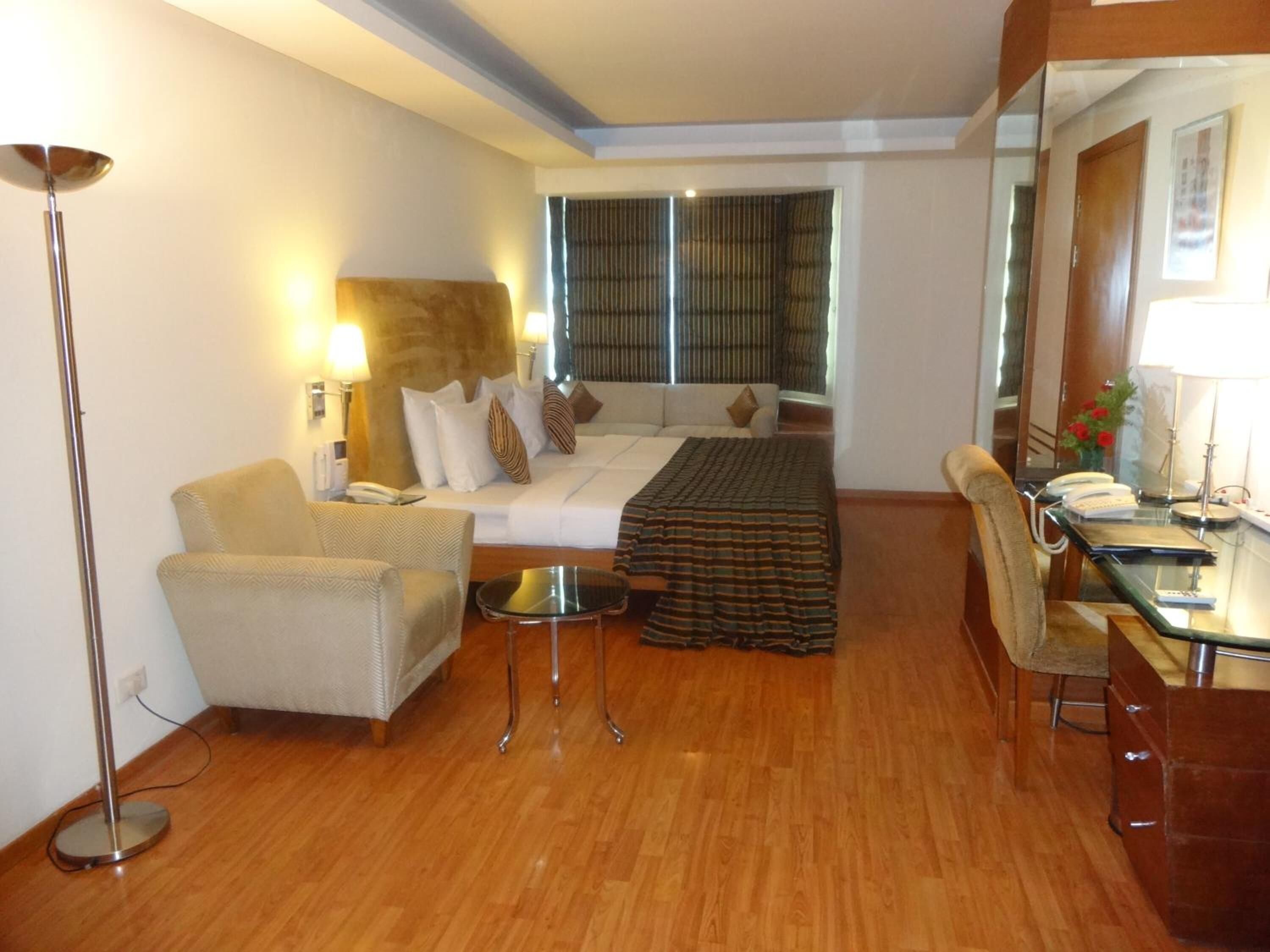 Quarto de hotel com sofá, poltrona, mesa de cabeceira e uma pequena mesa redonda.