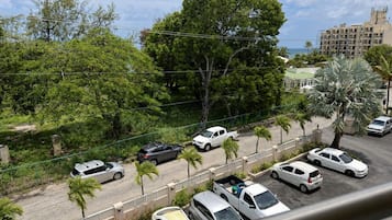 Um espaço de estacionamento com vários carros, um edifício ao fundo e uma árvore grande em primeiro plano.