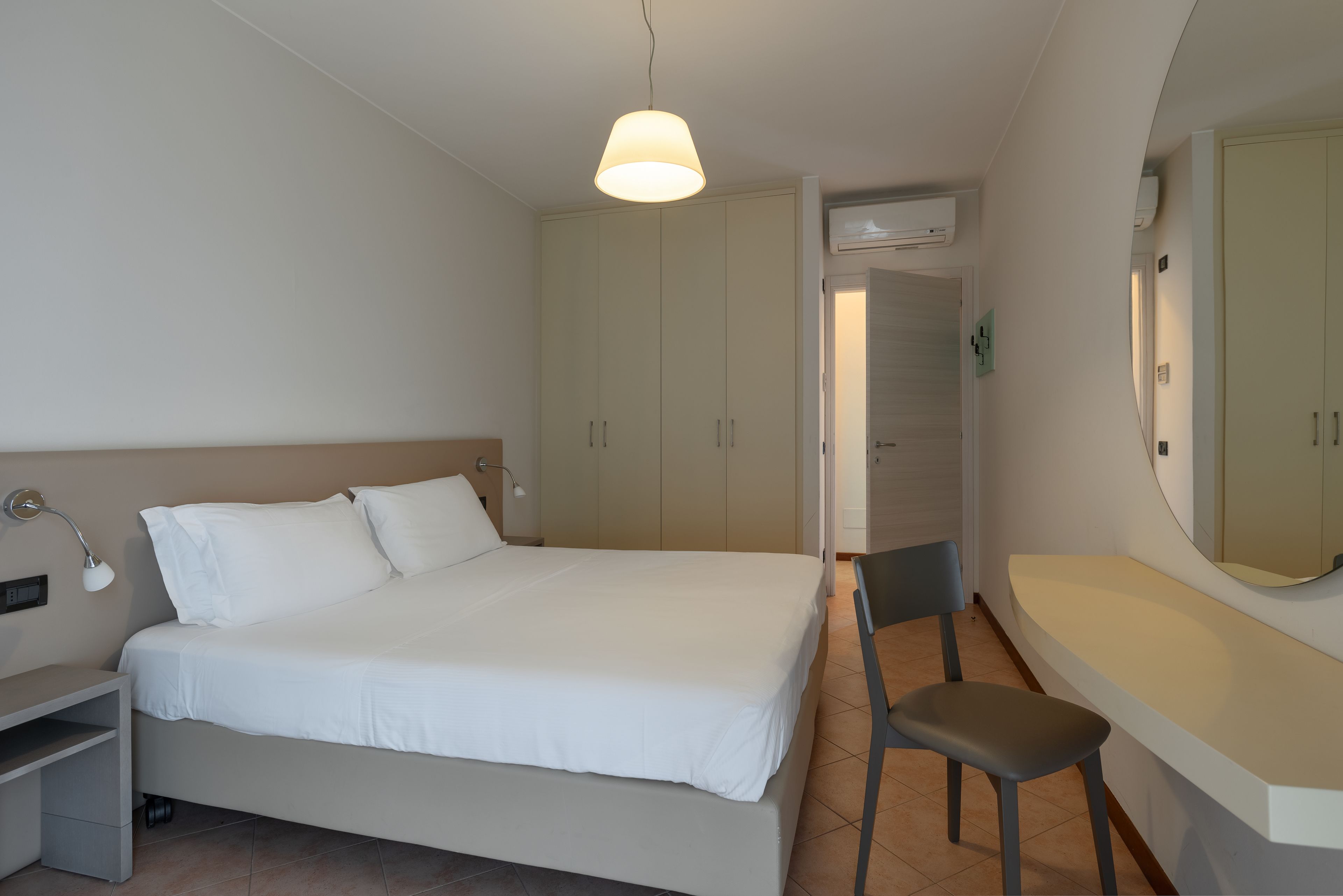 Um quarto com cama, mesa de cabeceira, cadeira e espelho.