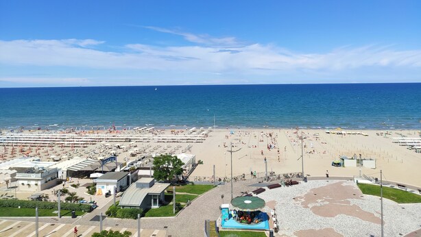 Um resort à beira-mar com uma extensa área de areia, uma piscina pequena e um palco para eventos.