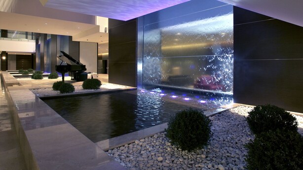 Espaço de piscina interior moderno, com piano, elemento aquático e uma grande parede com superfície refletora.