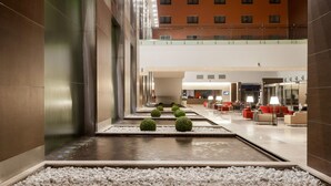 Um saguão moderno de hotel com um elemento central de água, áreas de estar e pé direito alto.