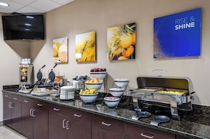 Disposição de buffet com diversos alimentos e uma televisão fixada na parede.