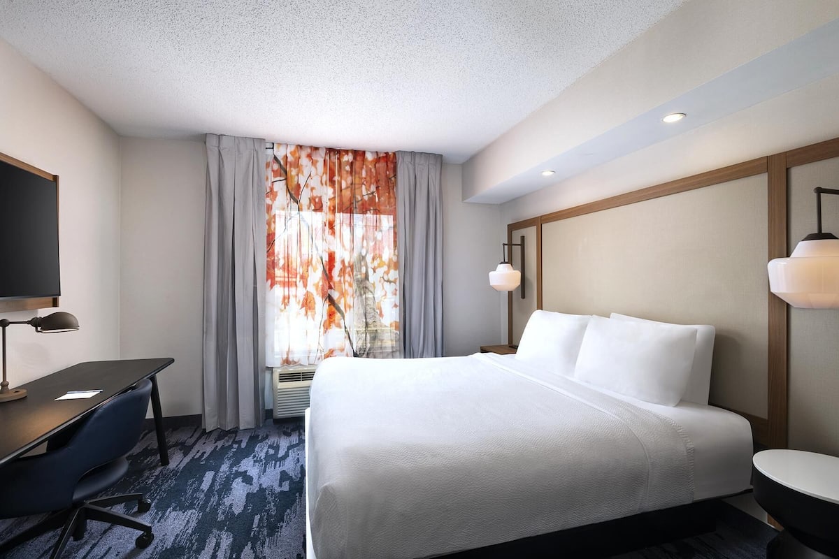 Quarto de hotel com uma cama, escrivaninha e televisão.