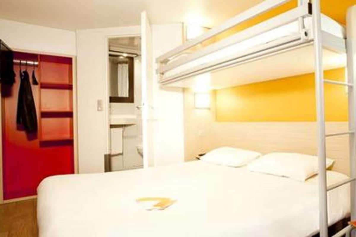 Quarto com beliche, guarda-roupa vermelho, espelho e uma mesinha.