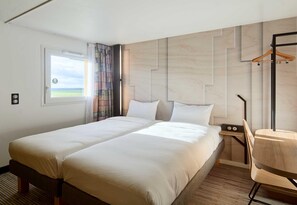 Quarto de hotel com cama, mesa pequena, cadeira, mesa de cabeceira e janela com vista.