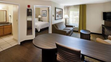 Quarto de hotel com área de jantar, cama, sofá, televisão e banheiro.